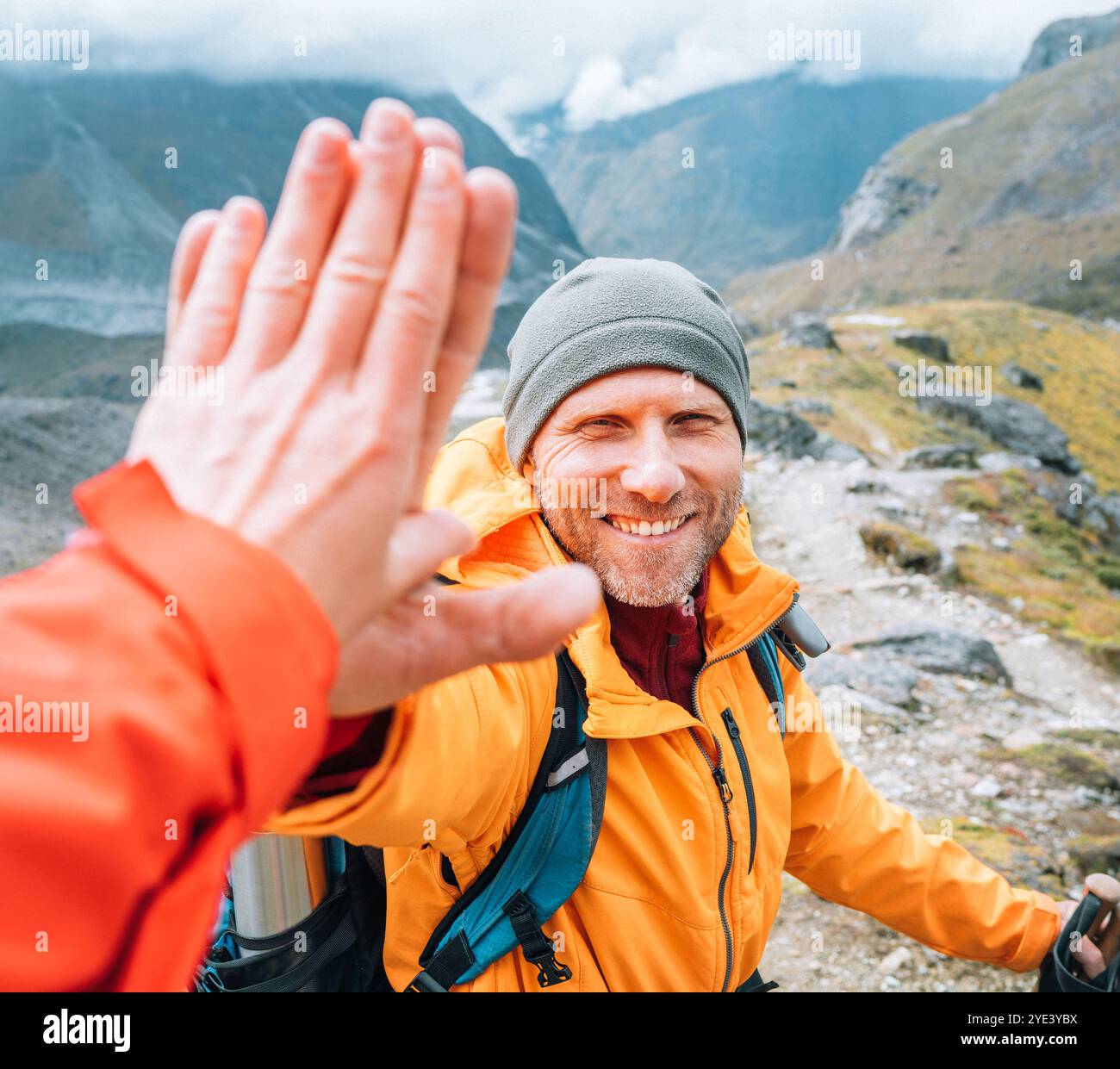 Smiling backpacker dressed orange jacket giving High Five to female ...
