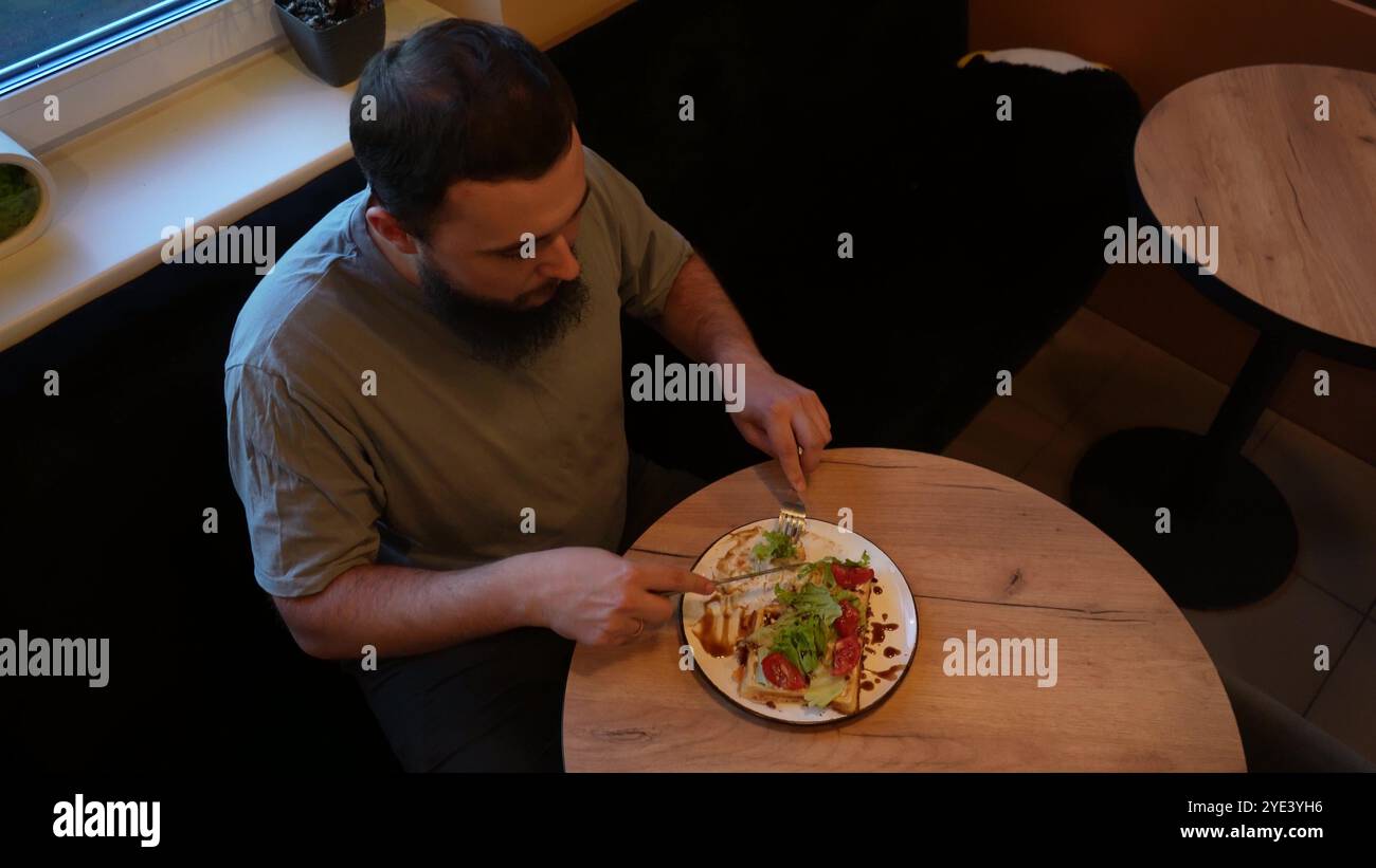 Bearded man eats at a cafe, taking in the cozy ambiance of warm ...