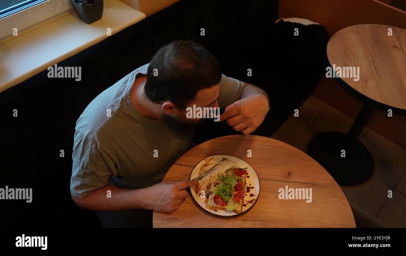 Bearded man eats at a cafe, taking in the cozy ambiance of warm ...