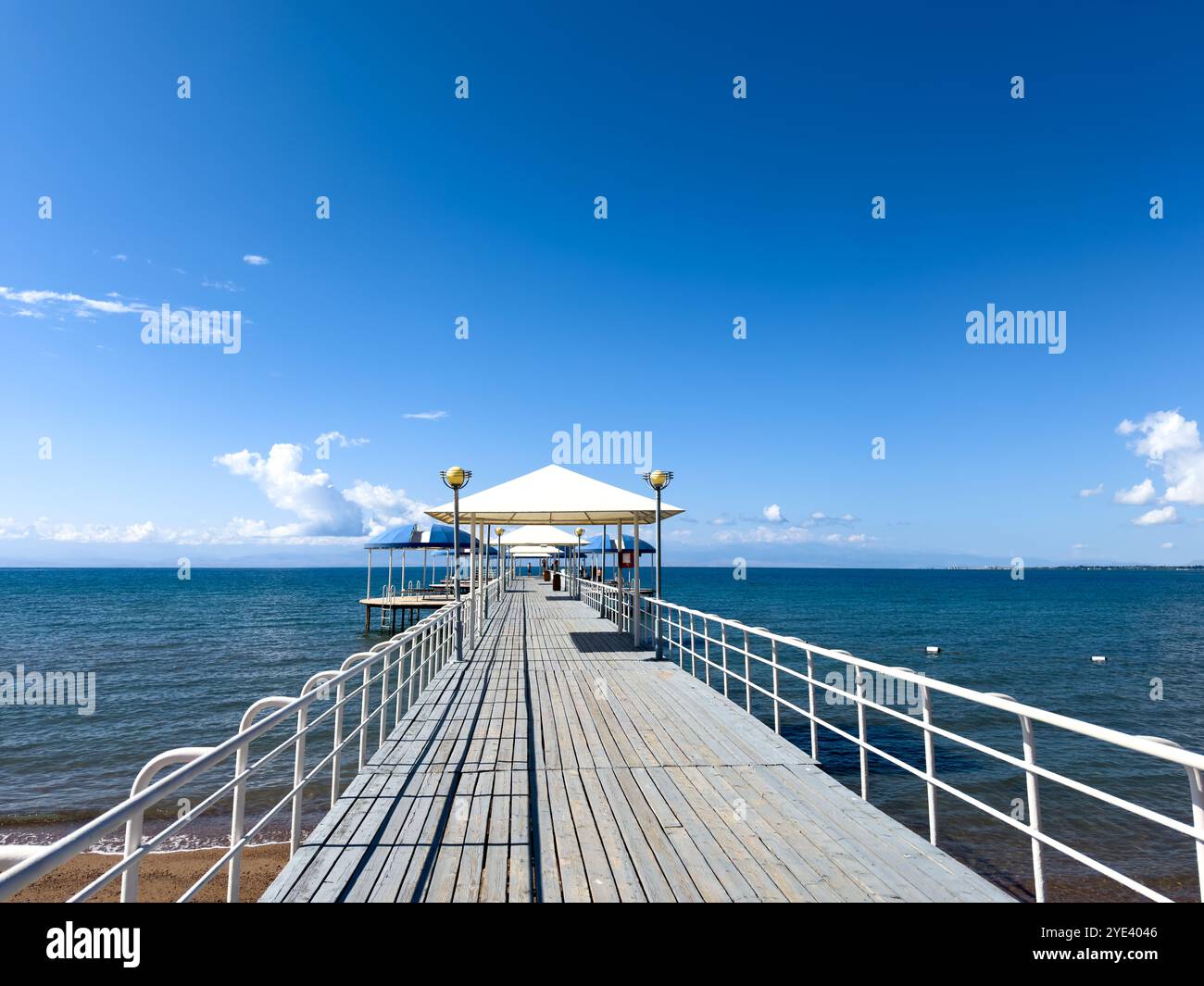A pier with white canopies stretches over the blue lake, extending into ...