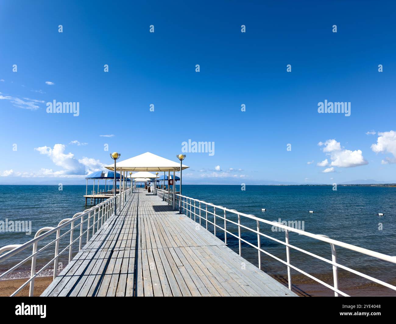 A pier with white canopies stretches over the blue lake, extending into ...