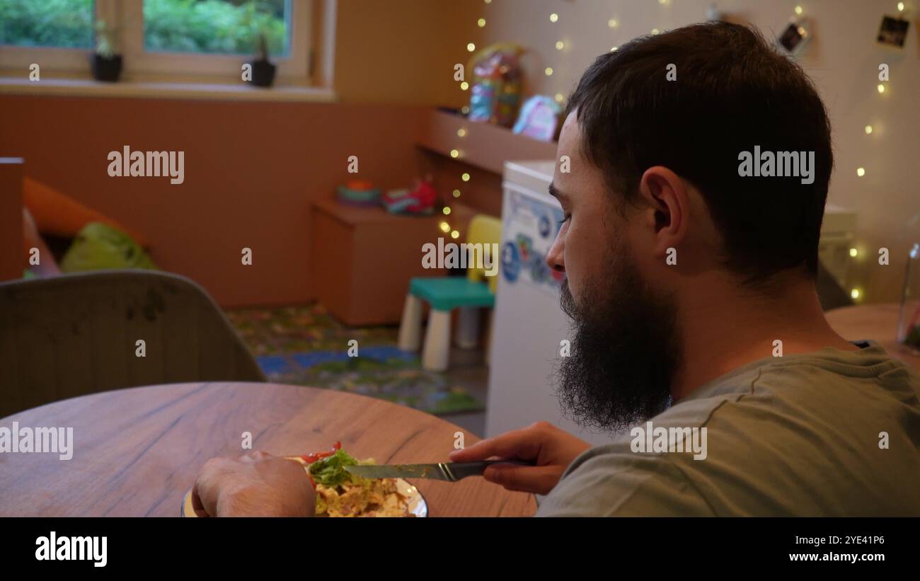 A man with a beard enjoys a meal, focused on his plate of food. Warm ...