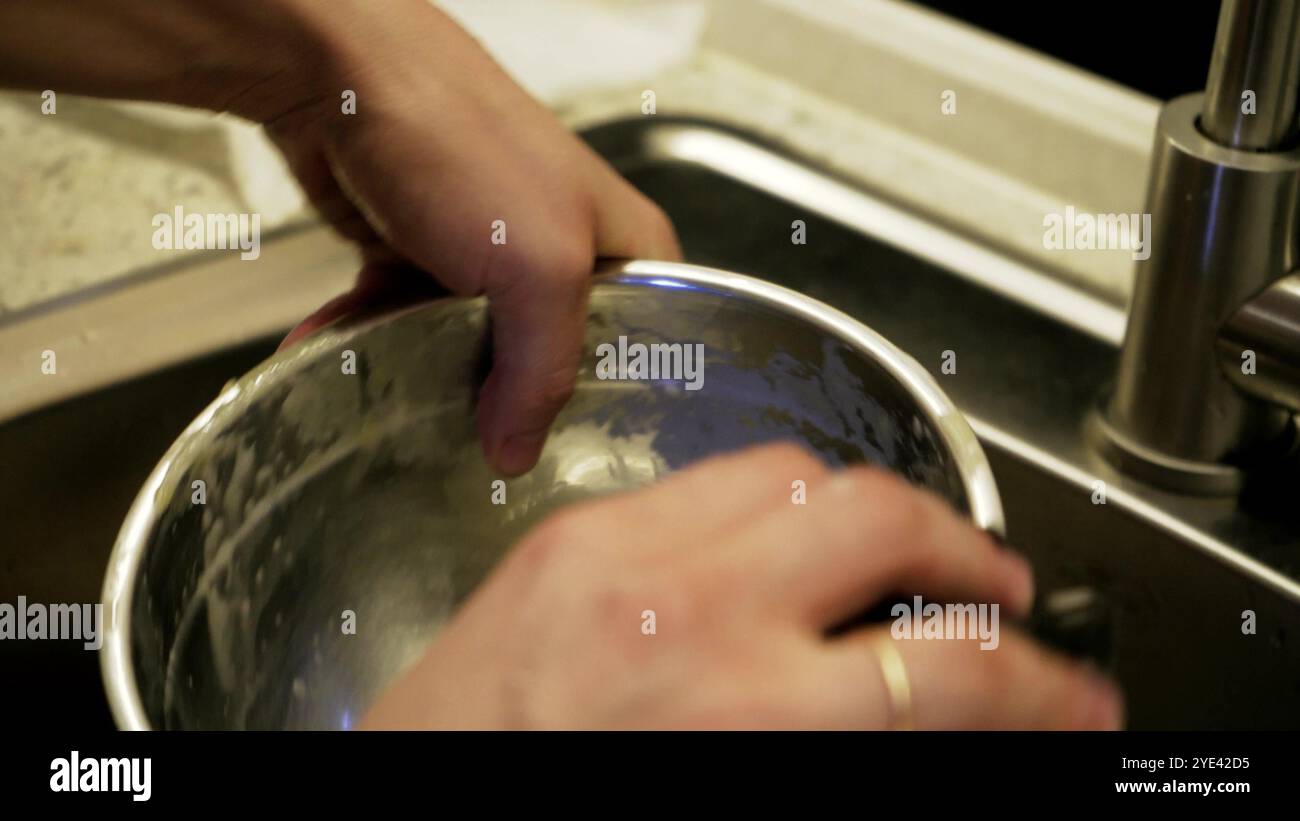 A close-up shot of hands washing a stainless steel bowl under running ...