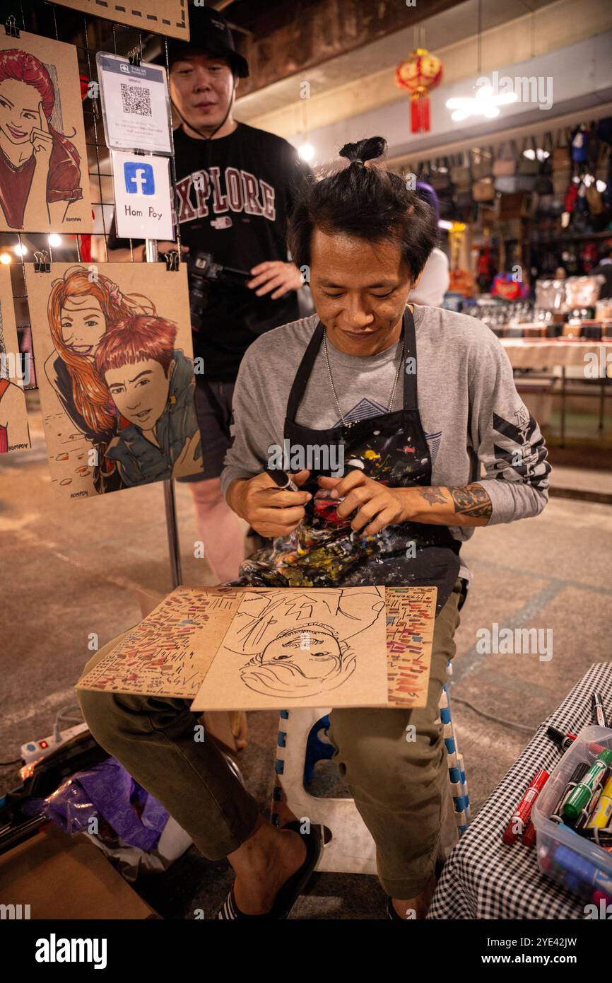 An artist draws portraits at the Chiang Rai night market, capturing the ...