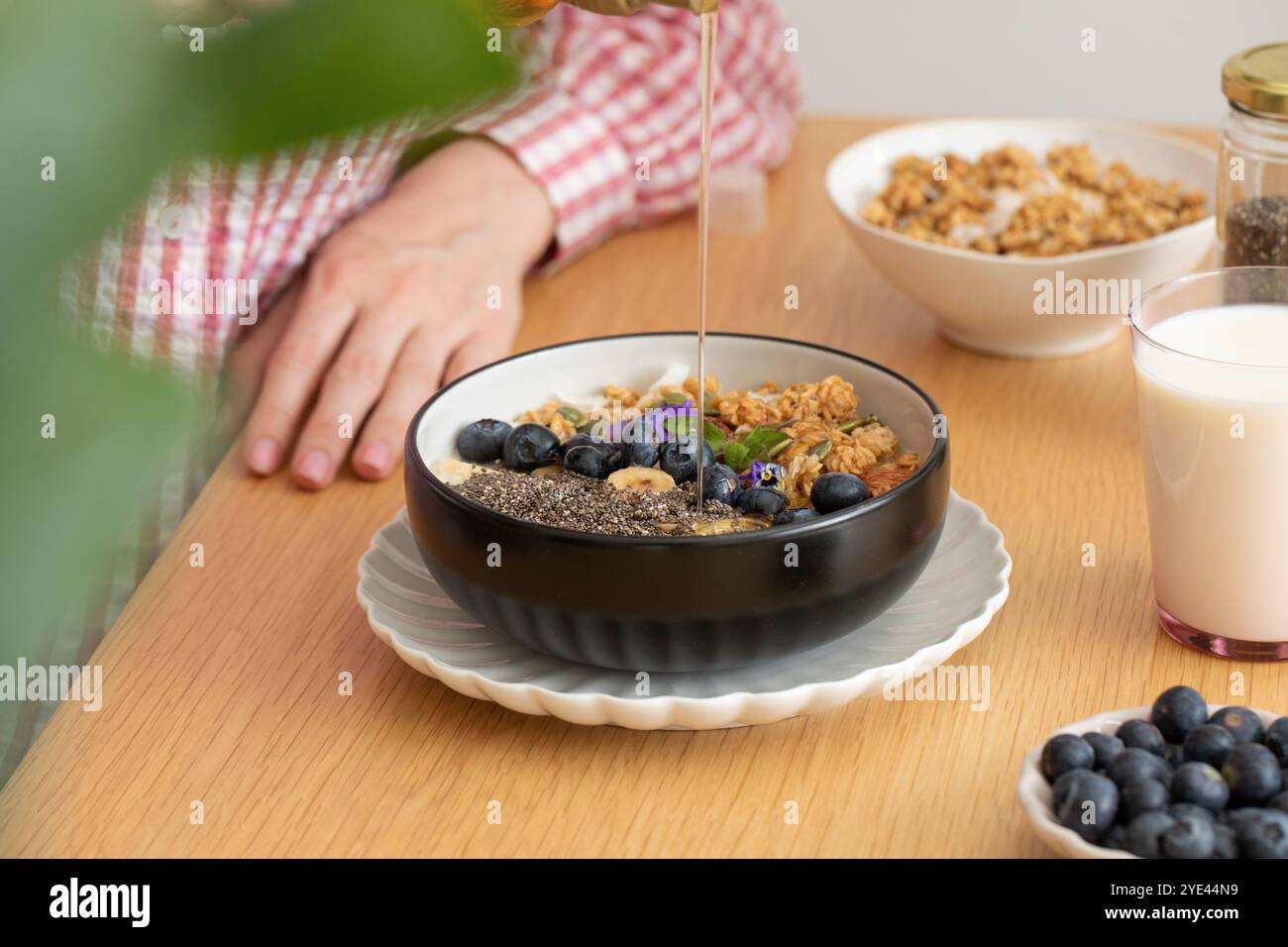 A woman pours maple syrup on granola and Greek yogurt. Healthy ...