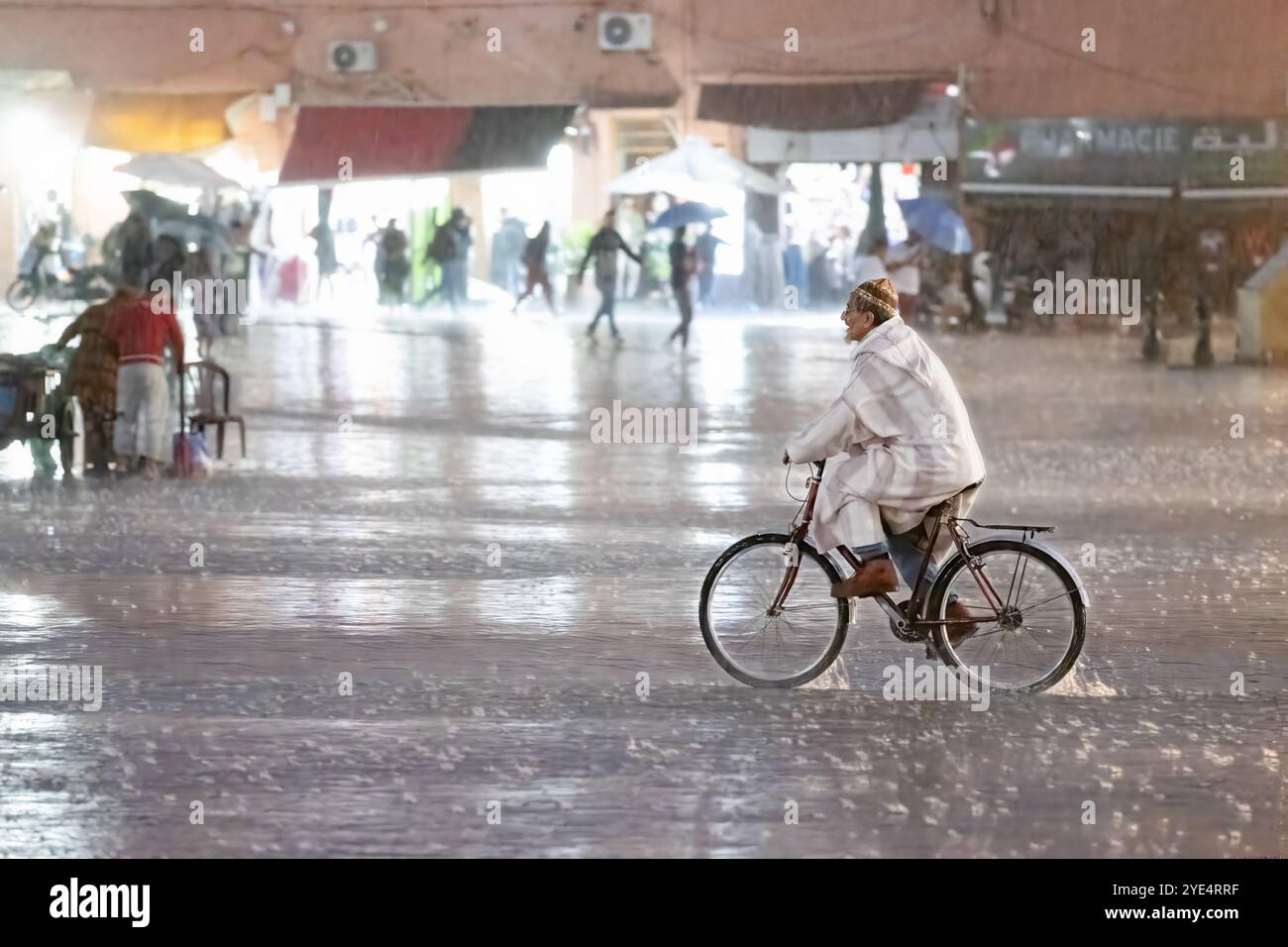 Marrakesh, Morocco. A soaking wet man cycles through Jemaa el-Fnaa, the ...