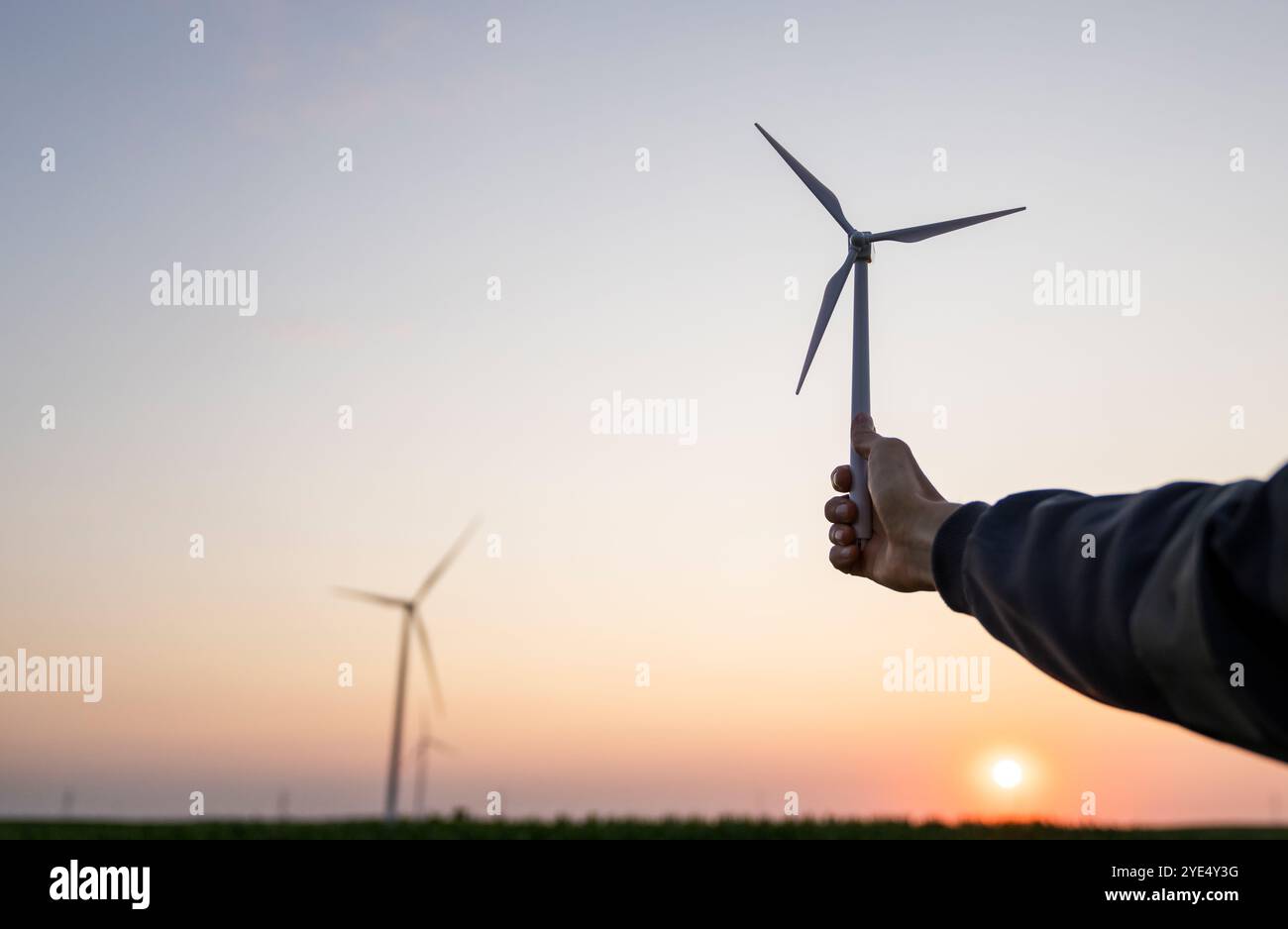 Man holds toy wind turbine in his hand. Real wind turbines in the ...