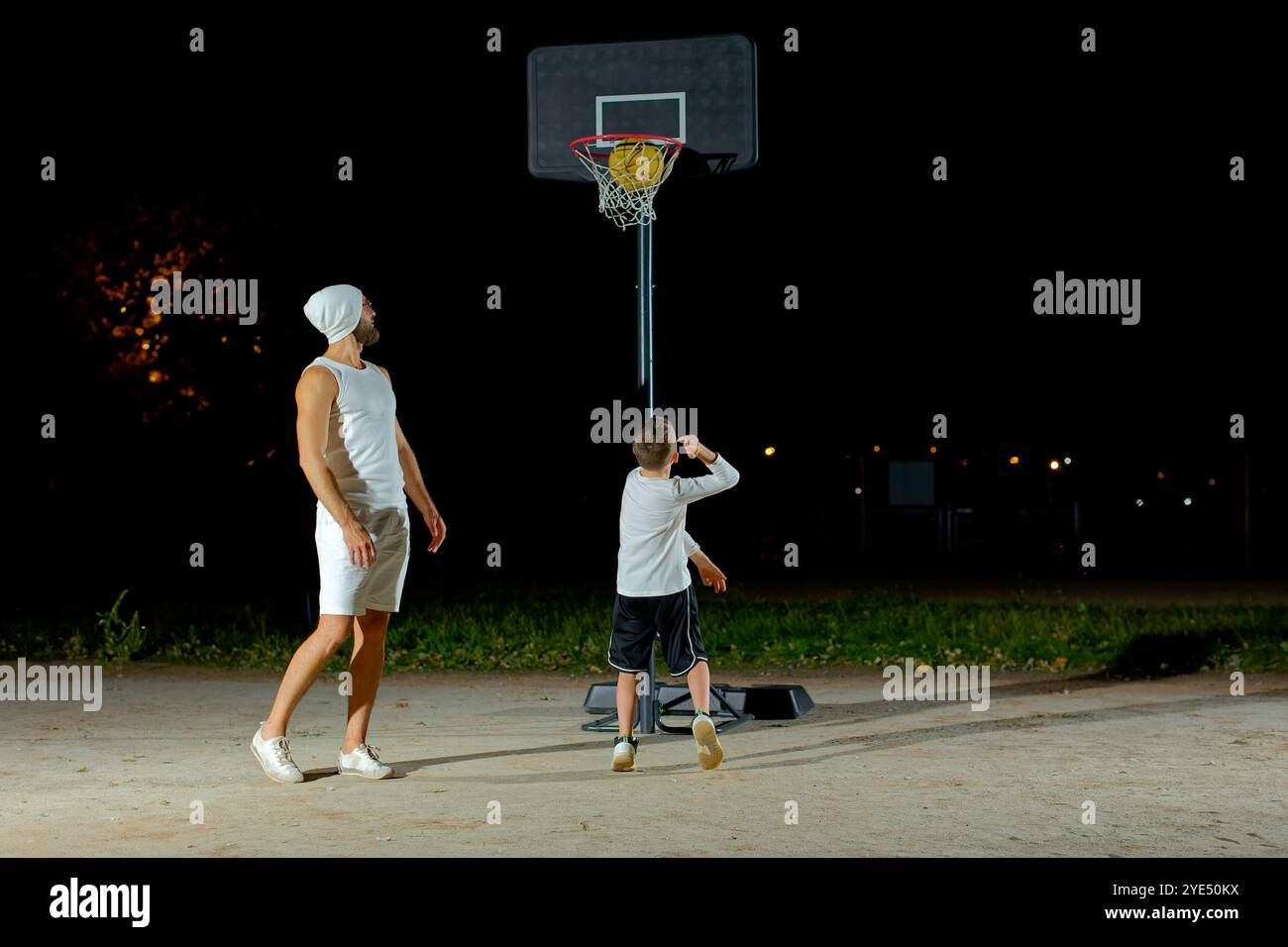 An adult and a young boy are playing basketball together at night ...