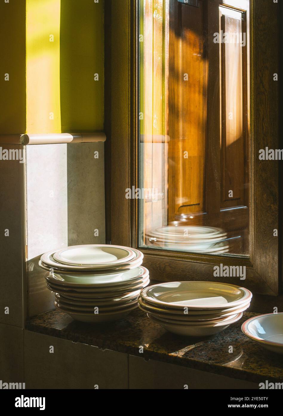 Stacks of white plates on a granite counter, bathed in warm sunlight ...
