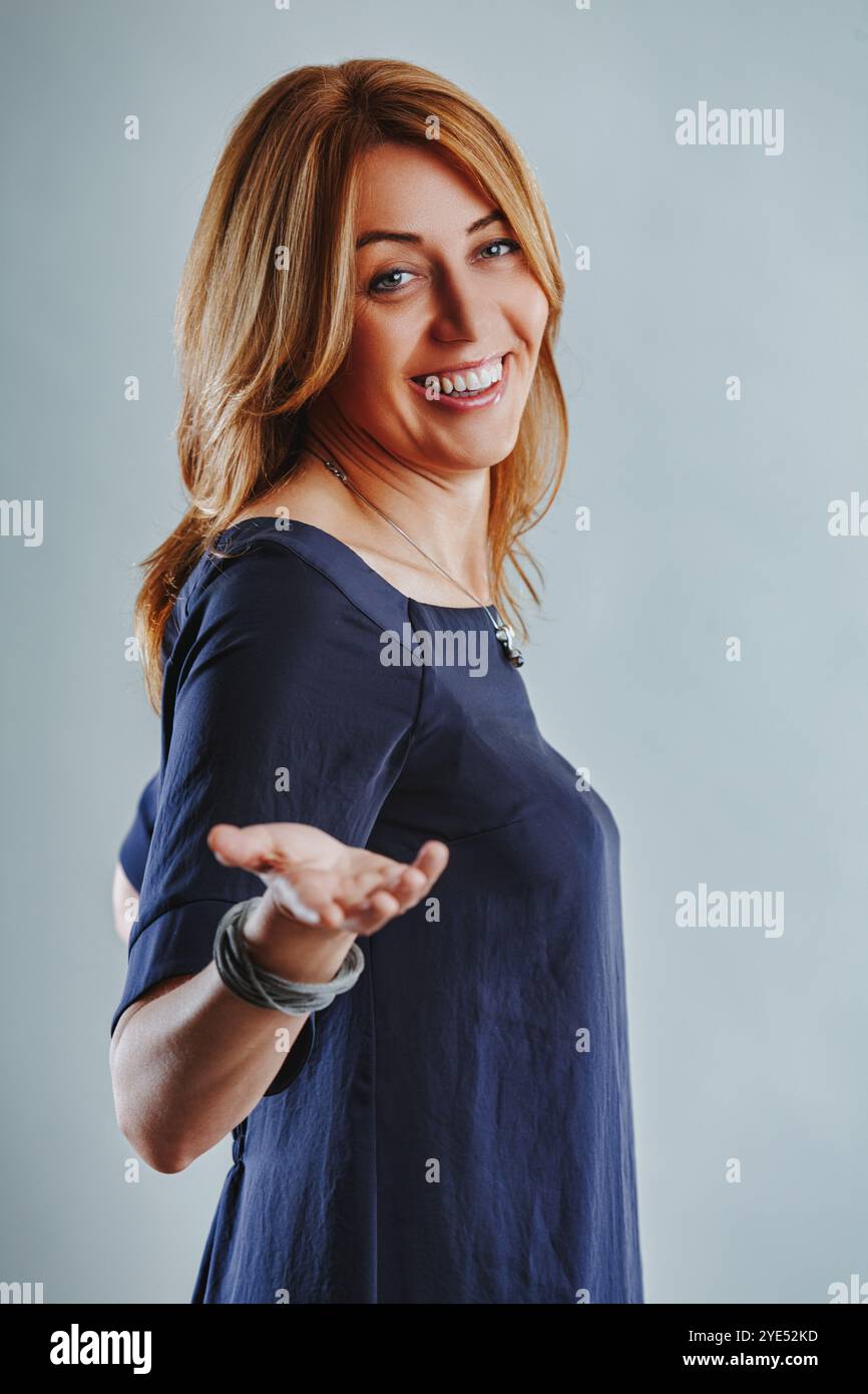 Cheerful businesswoman in her 40s, navy blue dress, open hand ...