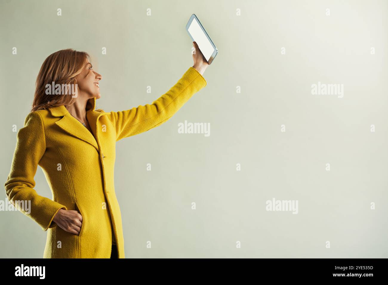Businesswoman wearing yellow coat holding tablet high up searching for ...