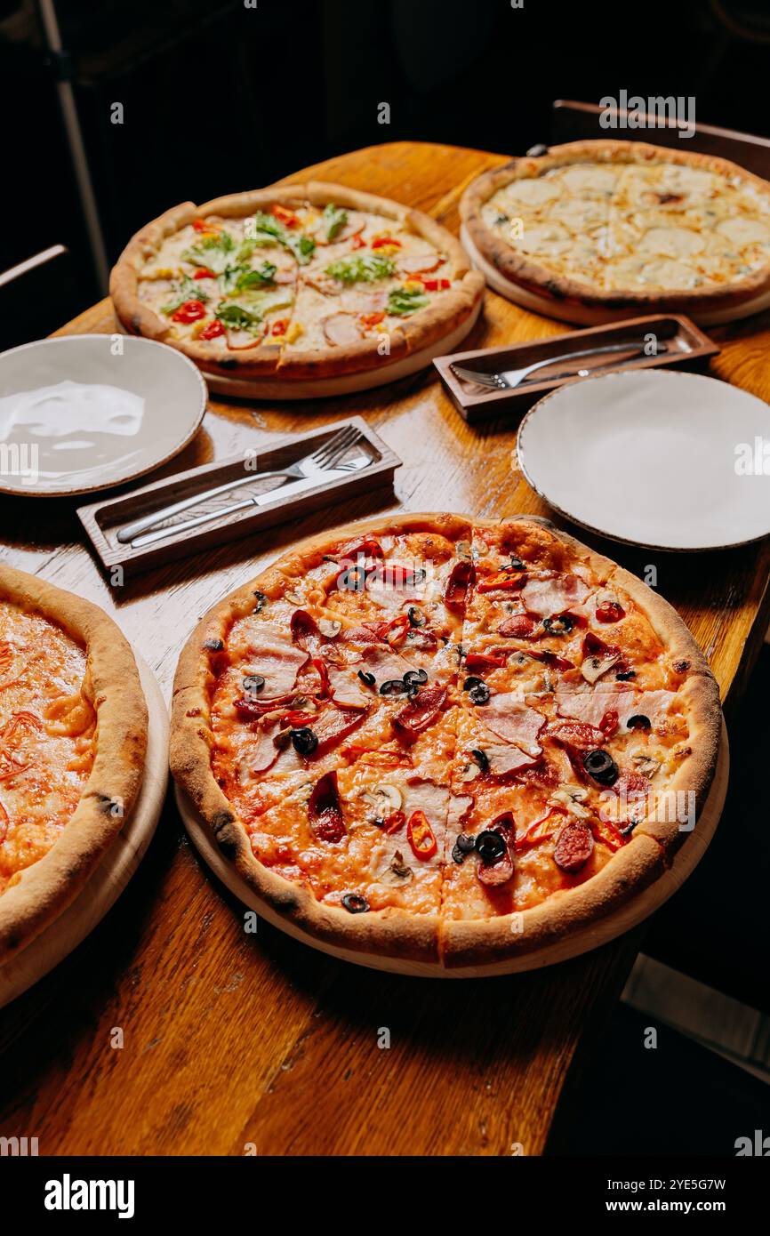 Assorted pizzas on a rustic wooden table, ready to serve with plates ...