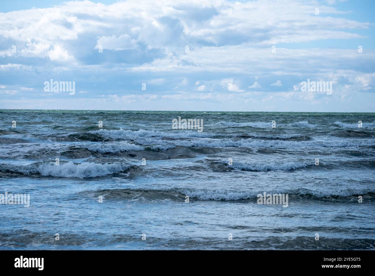 Gentle waves roll onto the sandy shore as clouds drift overhead in a ...