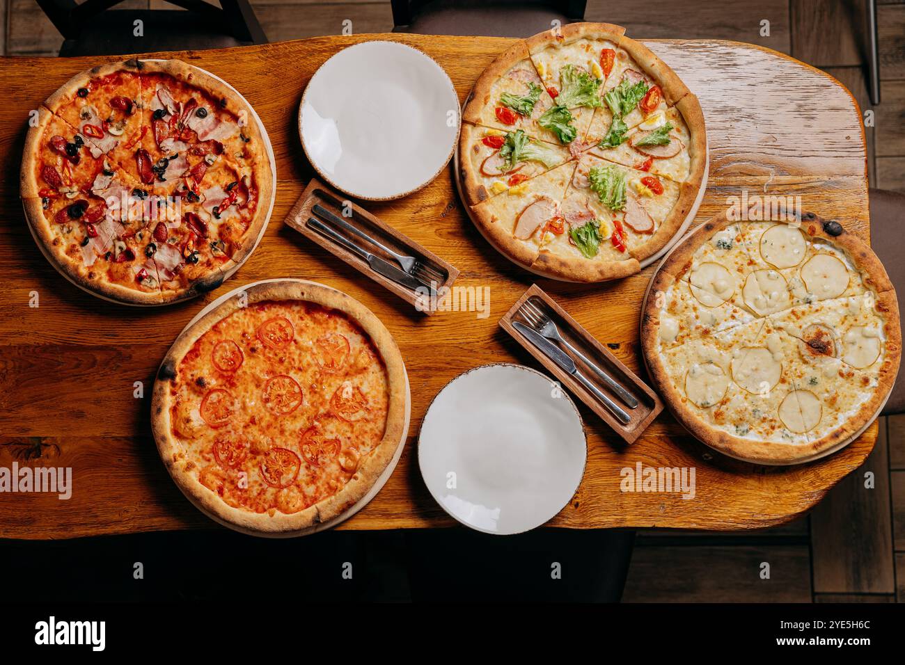 Assorted pizzas on a rustic wooden table, ready to serve with plates ...
