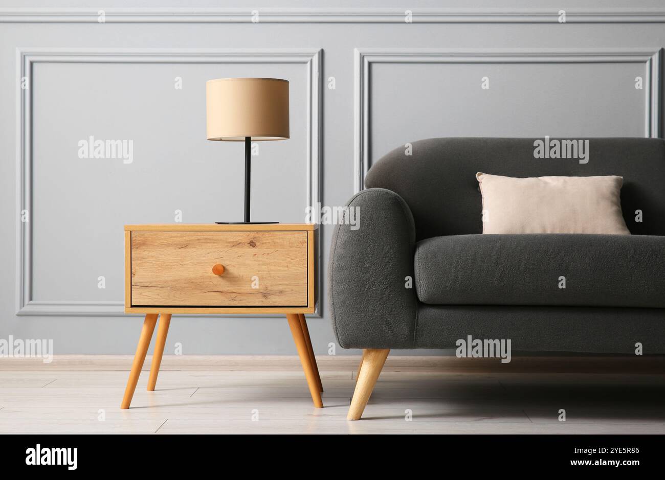 Stylish sofa with cushion and lamp on side table near grey wall Stock ...