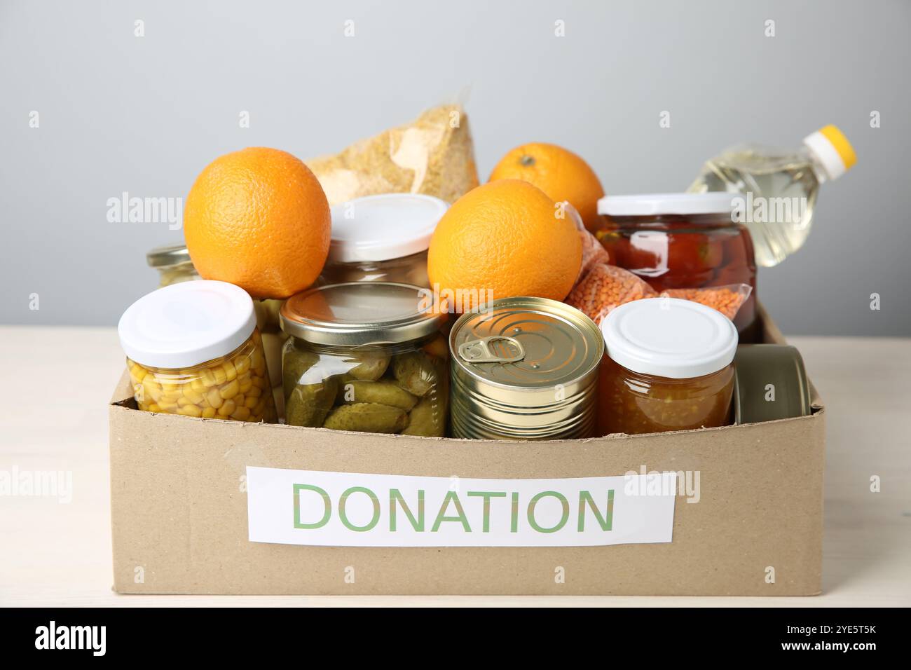 Different food products for donation in box on table against grey ...
