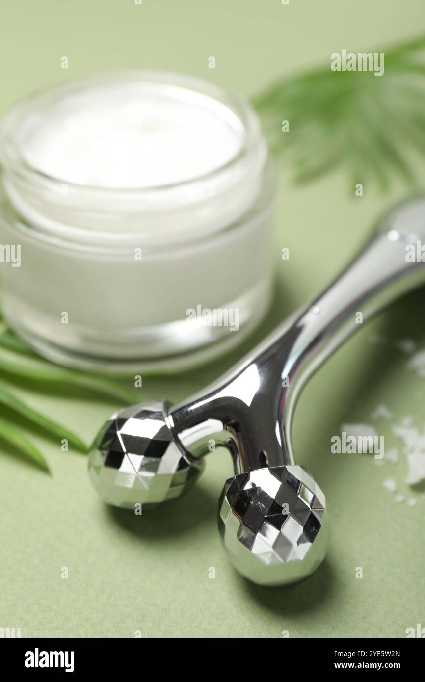 Metal face roller and cosmetic product on green background, closeup ...