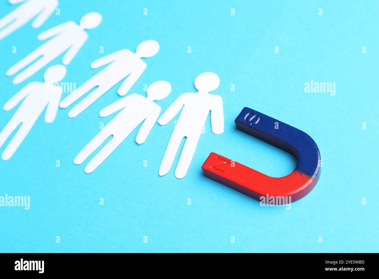 Magnet attracting paper cutouts of humans on light blue background ...