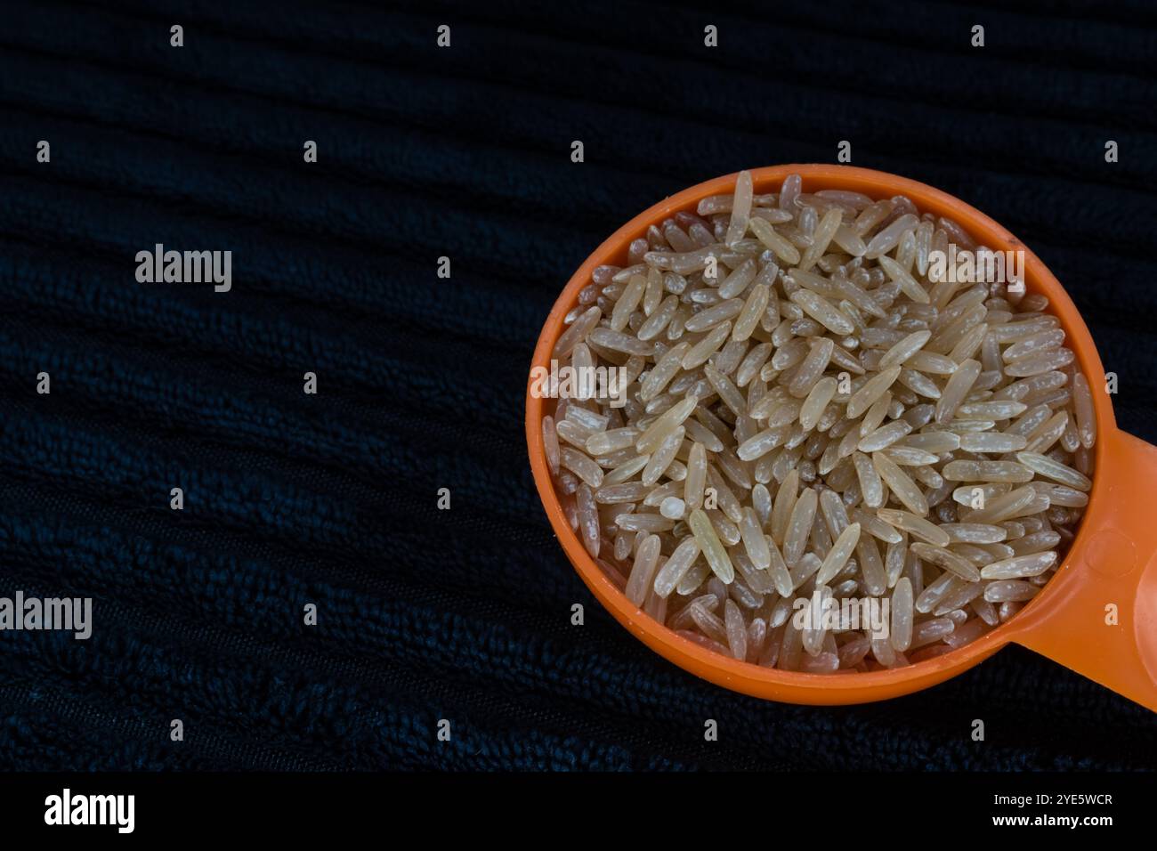 Raw grains of brown rice in measuring spoon on a black background with ...