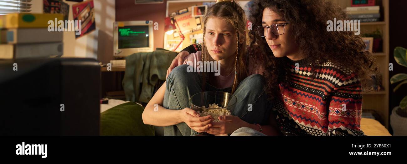 Two friends watching movie on television while sitting on couch. One ...