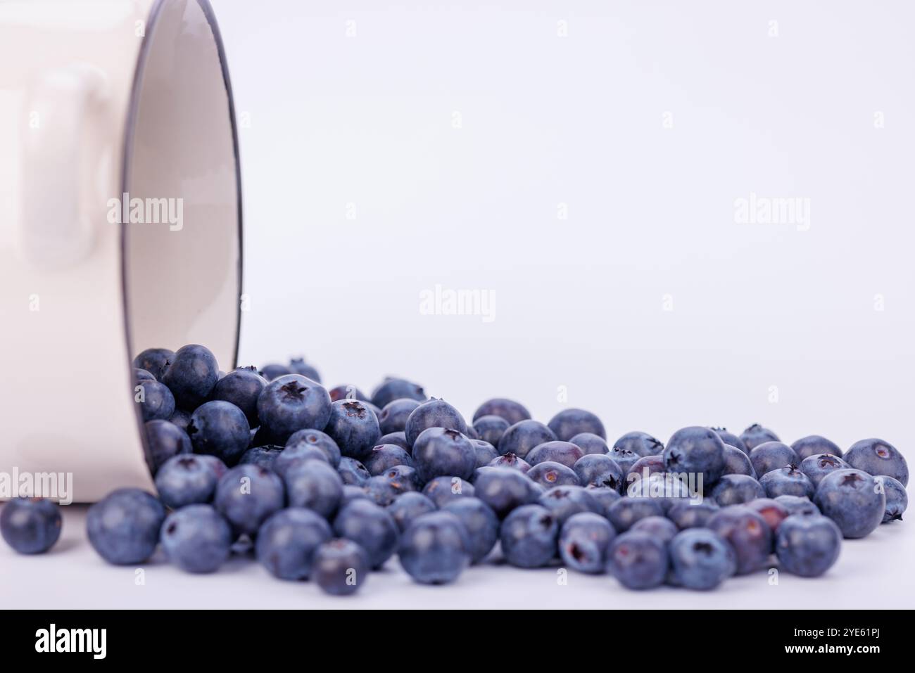 A detailed shot of a bowl of blueberries spilled on a white surface ...