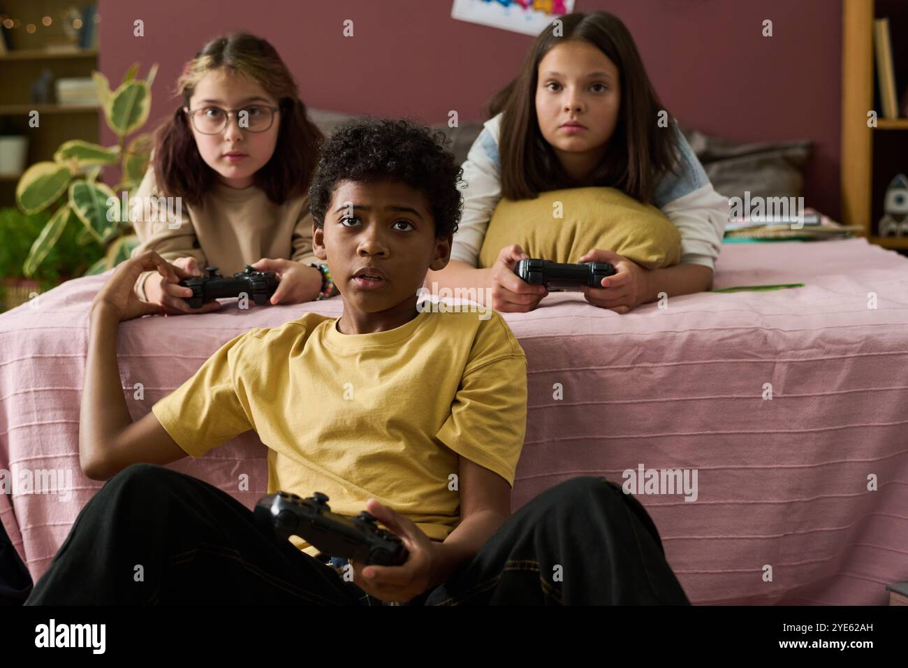 Three children lying on a bed, engrossed in playing video games with ...