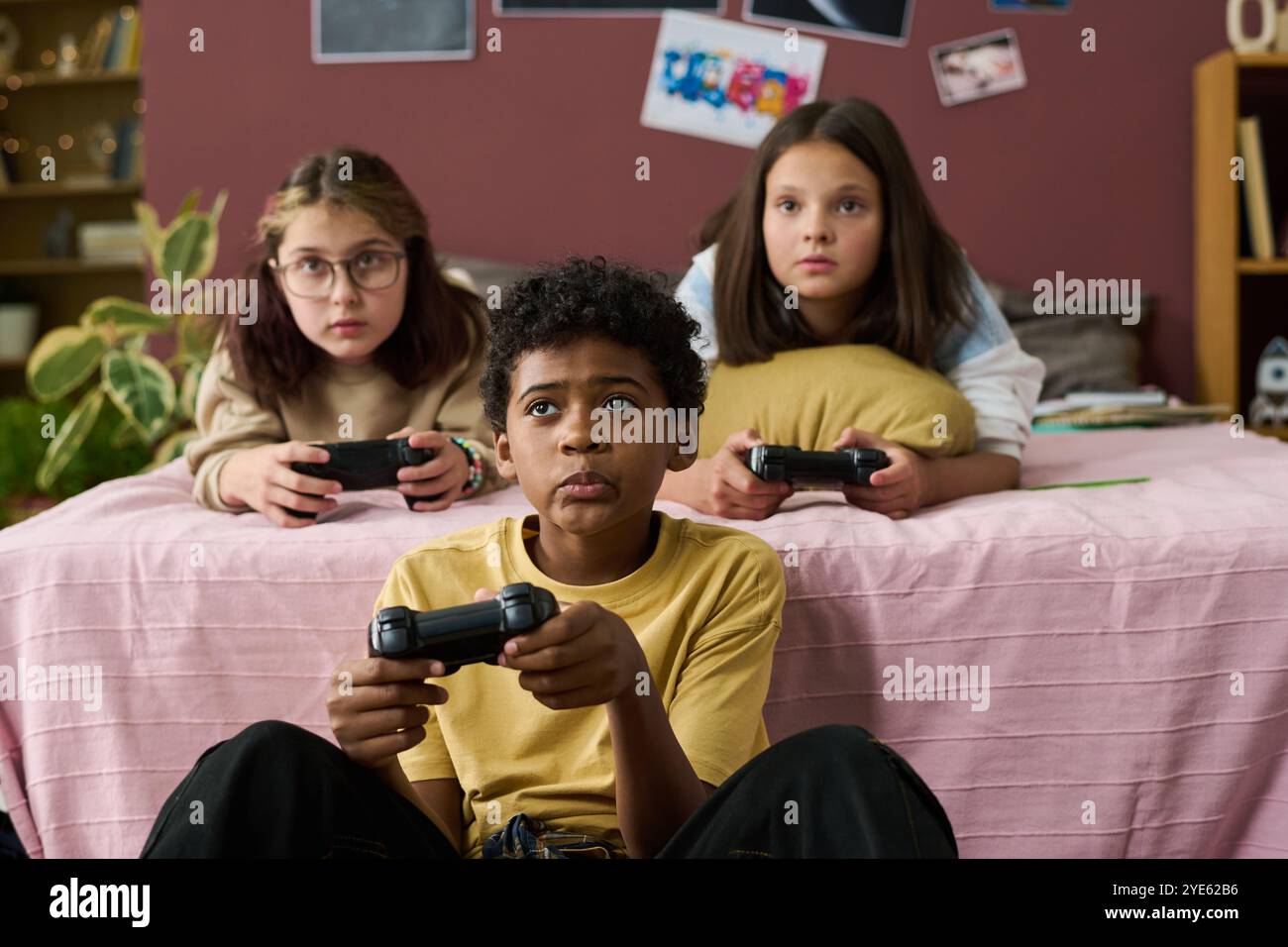 Kids focused on playing video games in living room with friends gazing ...