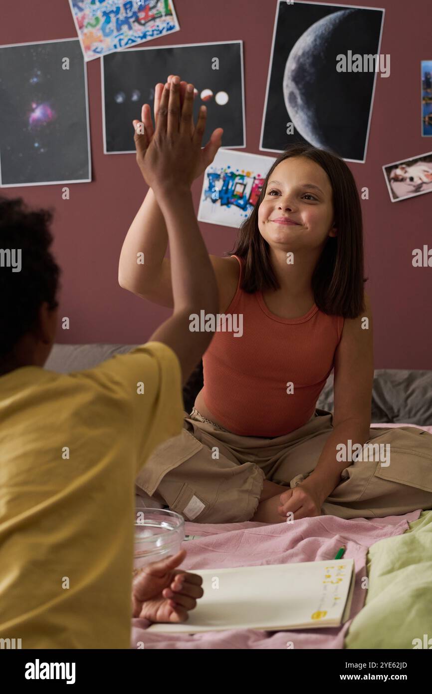 Two children high-fiving while sitting on a bed with space themed ...