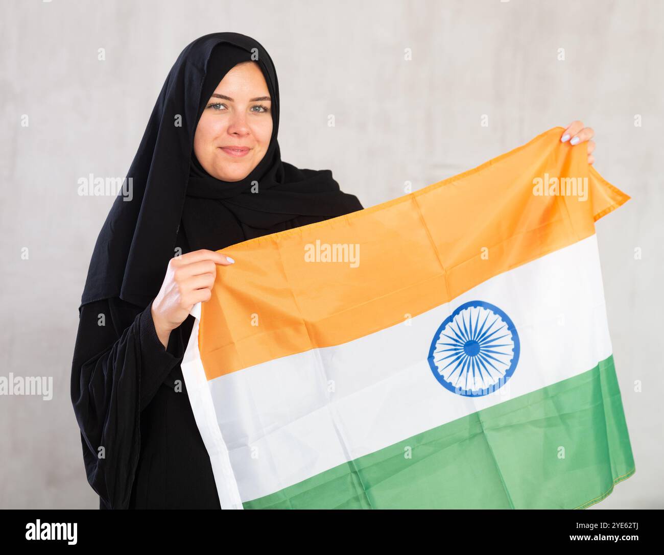 Balanced smiling Muslim woman in traditional black hijab holds flag of ...