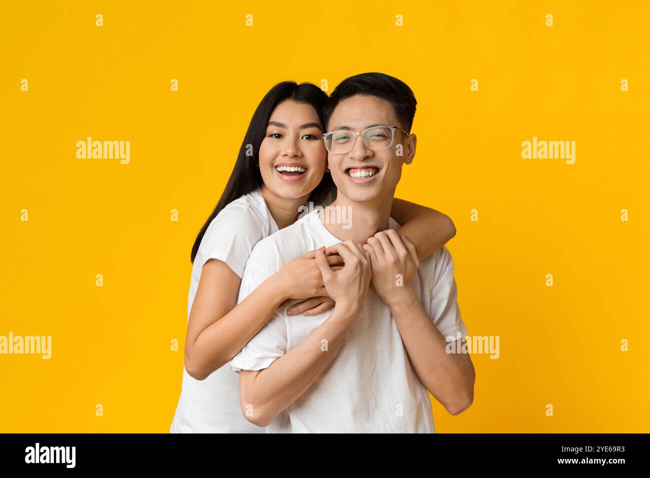 Emotional asian girl hugging her boyfriend over yellow background Stock Photo - Alamy