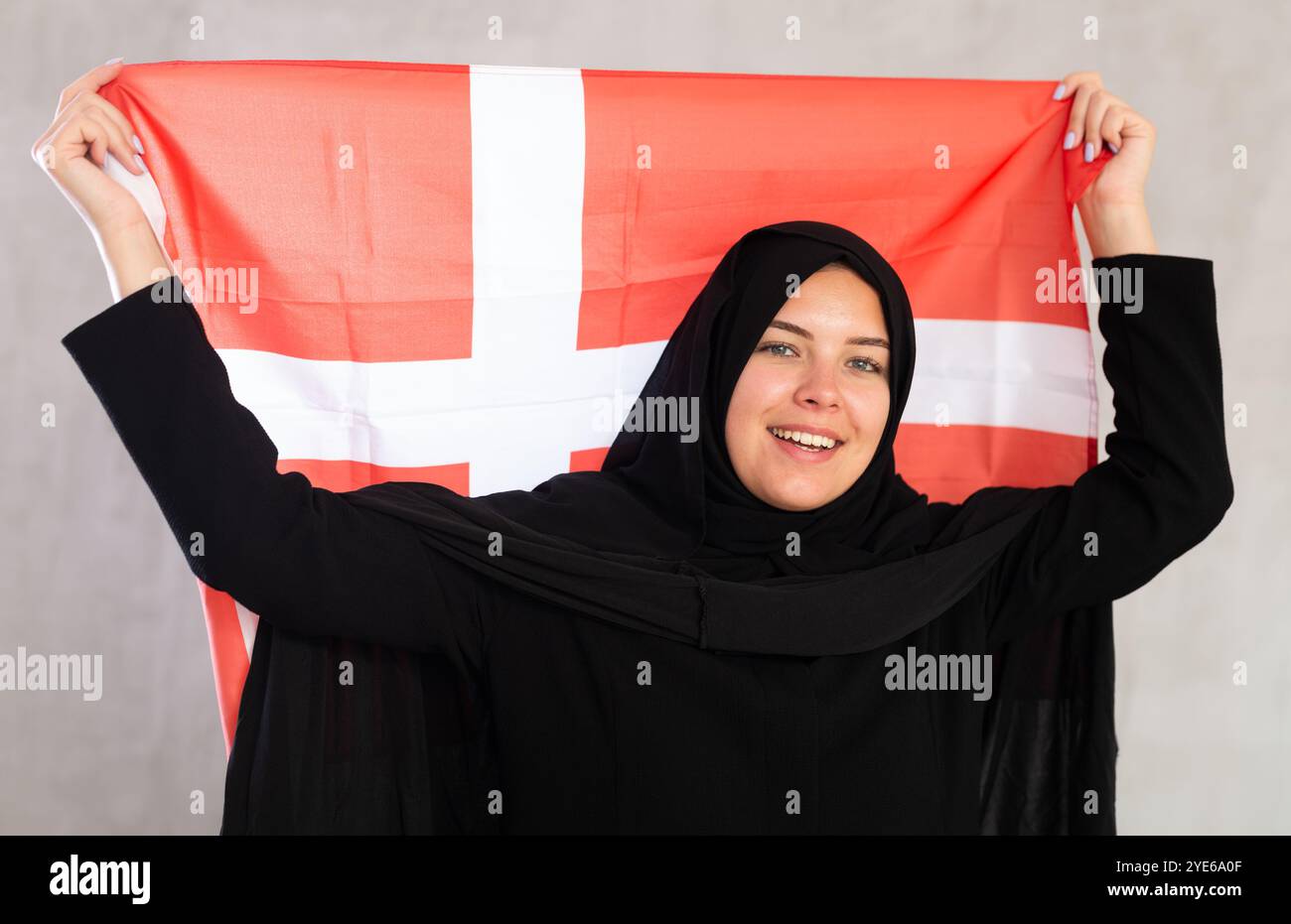 Balanced smiling Muslim woman in traditional black hijab holds flag of ...