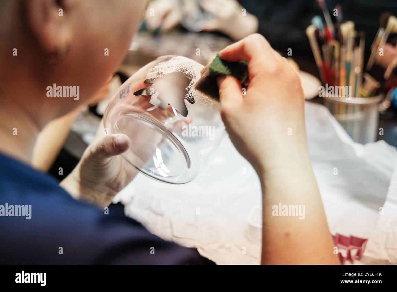 An artisan carefully applies a design to a glass using a sponge ...