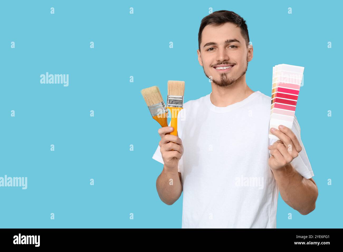 Young man with color palettes and paint brushes on blue background ...