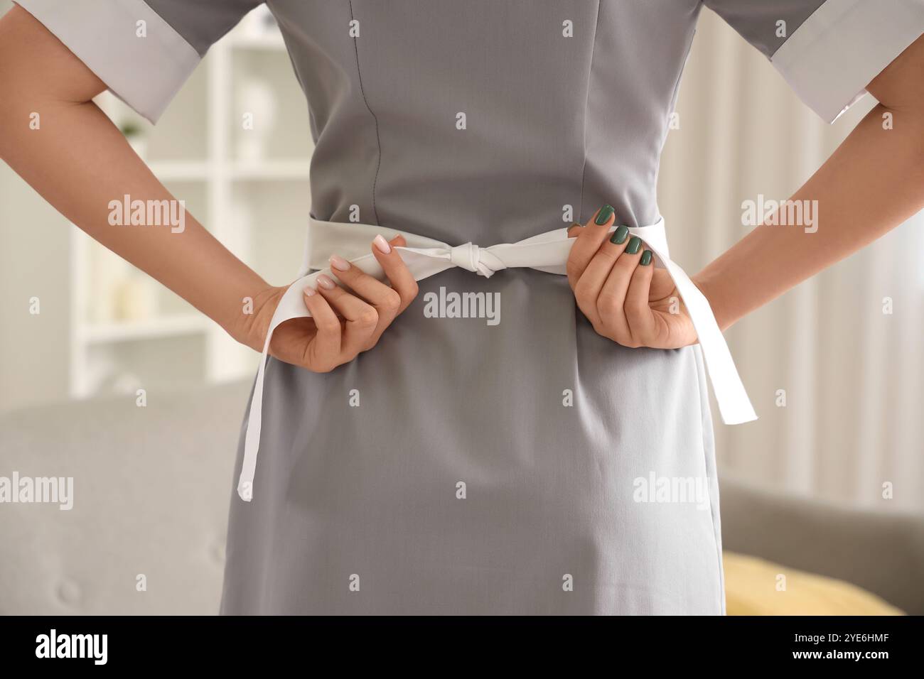 Young housemaid tying apron in room, back view Stock Photo - Alamy