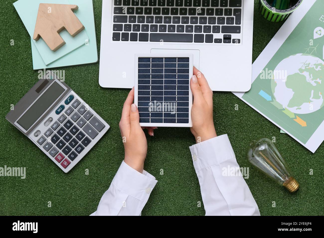 Woman with solar panel, laptop, calculator and light bulb on grass ...