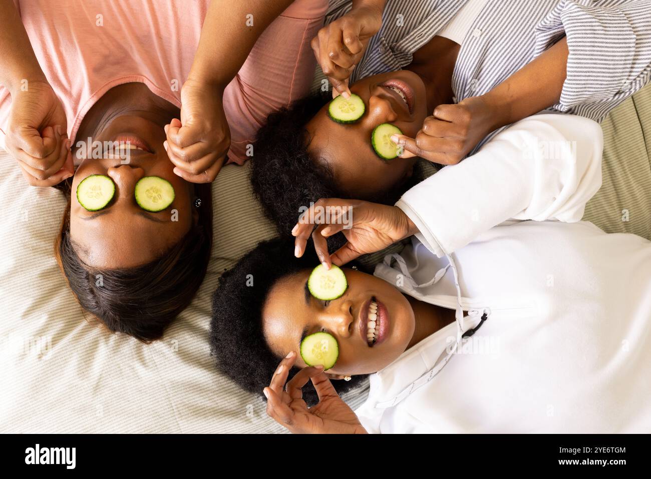 African american female friends relaxing with cucumber slices on eyes, enjoying spa day at home ...