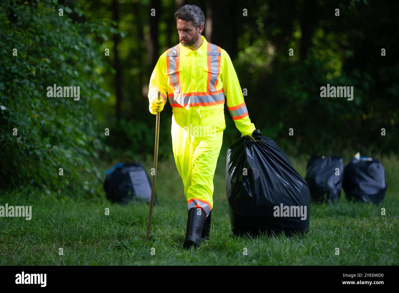 Volunteer man collecting garbage, picking up waste at nature. Land pollution, environmental ...