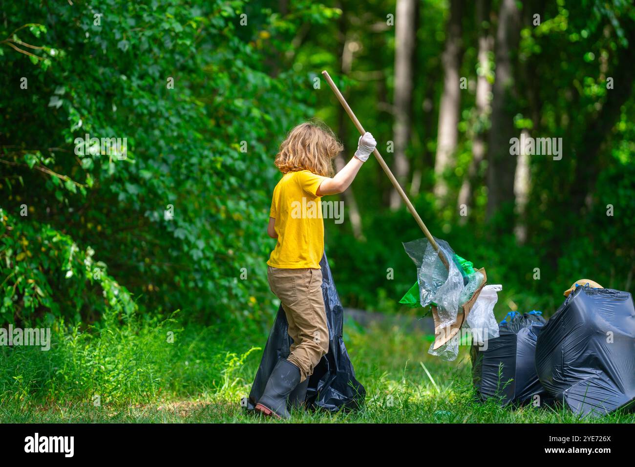 Kid cleaning up the park, putting trash in a garbage bag. Environmental ...