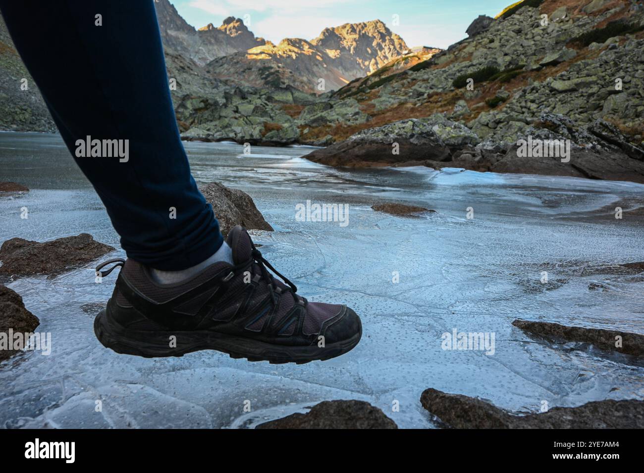 Hiker carefully placing foot on thin ice covering mountain lake in ...