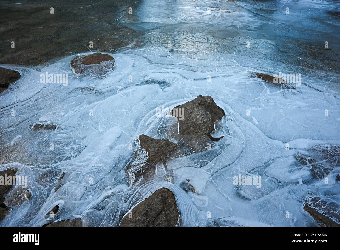 Thin layer of ice forming unique patterns on water surface with rocks ...