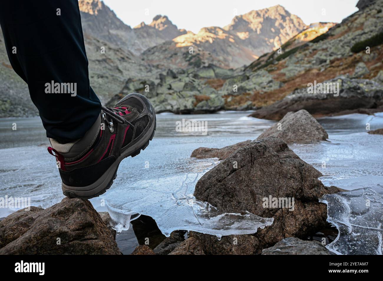 Hiker carefully placing foot on thin ice covering mountain lake in ...