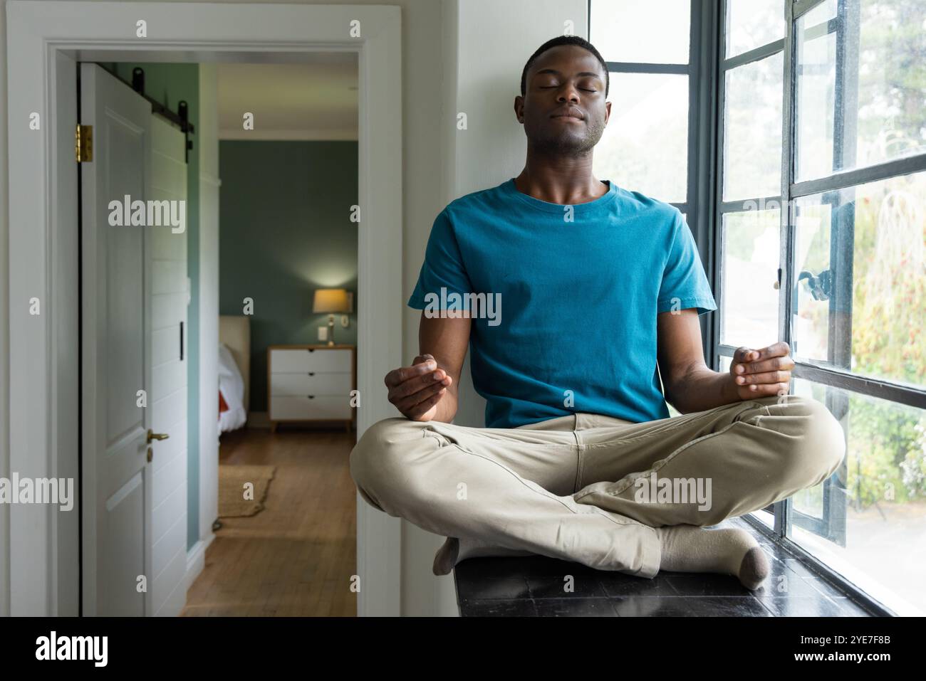 African American man meditating by window at home, finding inner peace ...
