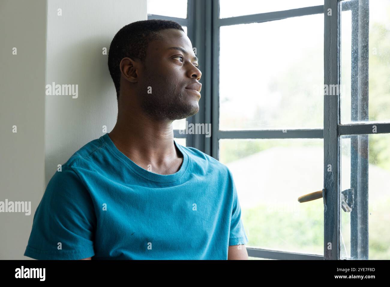 African American man gazing out window, reflecting peacefully at home ...