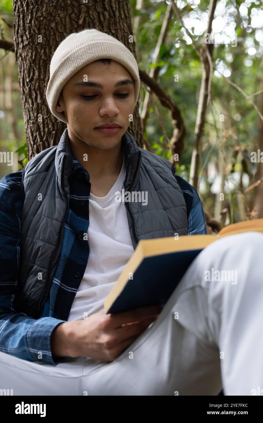 Young man reading book outdoors, relaxing against tree in peaceful ...