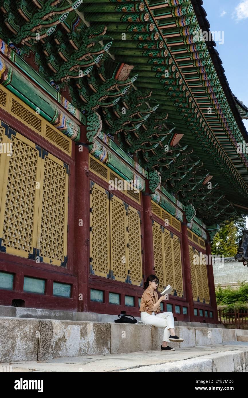 Korean girl reading book seated with traditional Korean temple ...