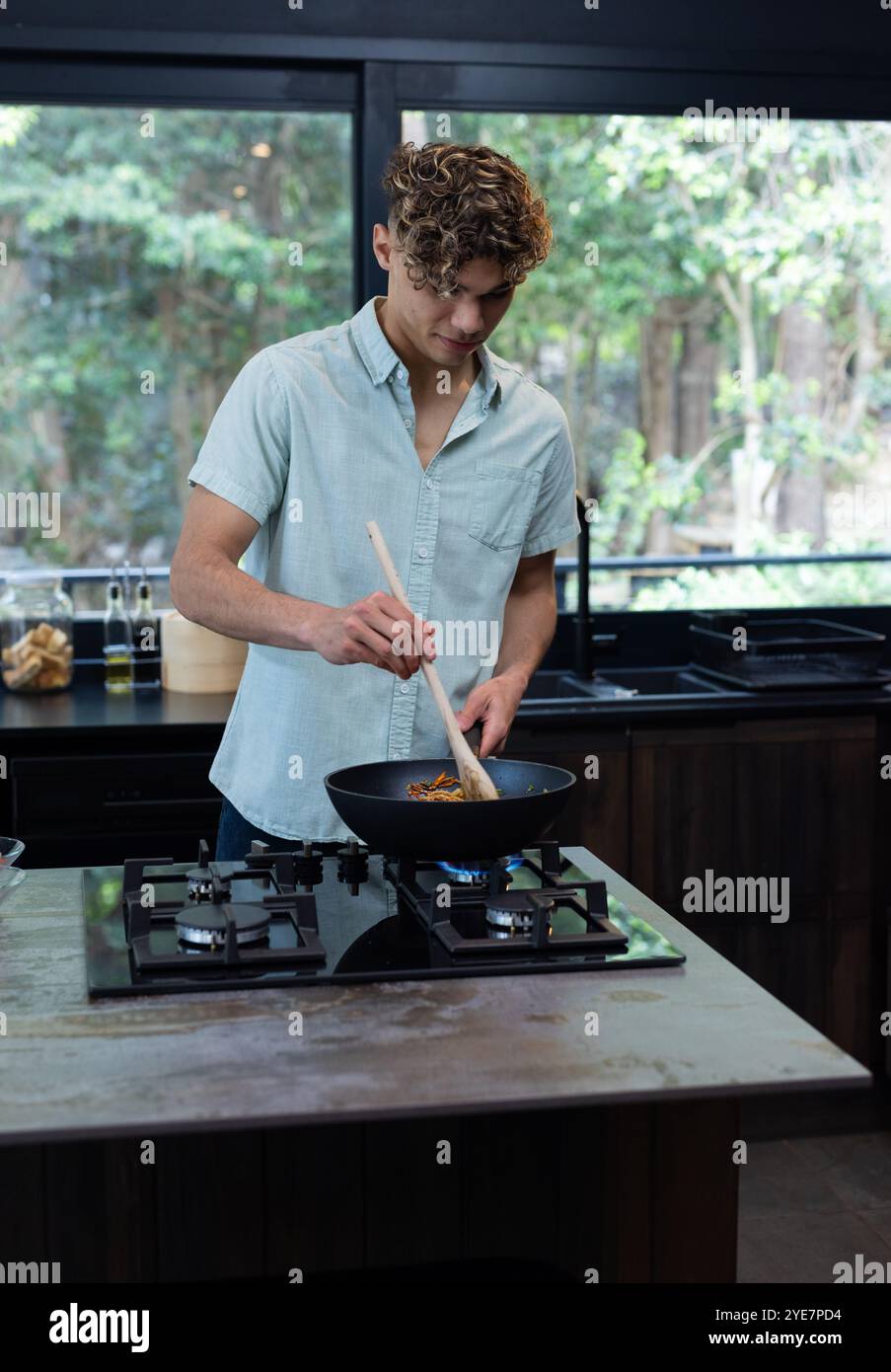 Young man cooking in modern kitchen, stirring vegetables in frying pan ...