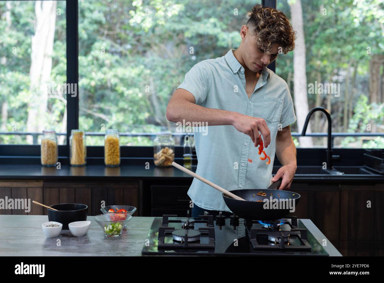 Young man cooking in modern kitchen, adding red peppers to stir-fry, at ...