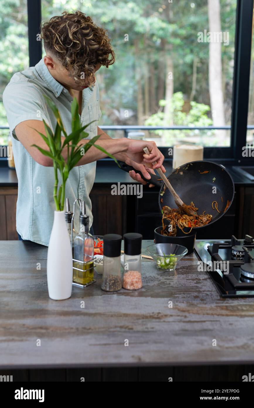 Man cooking noodles in modern kitchen, adding vegetables from wok, at ...