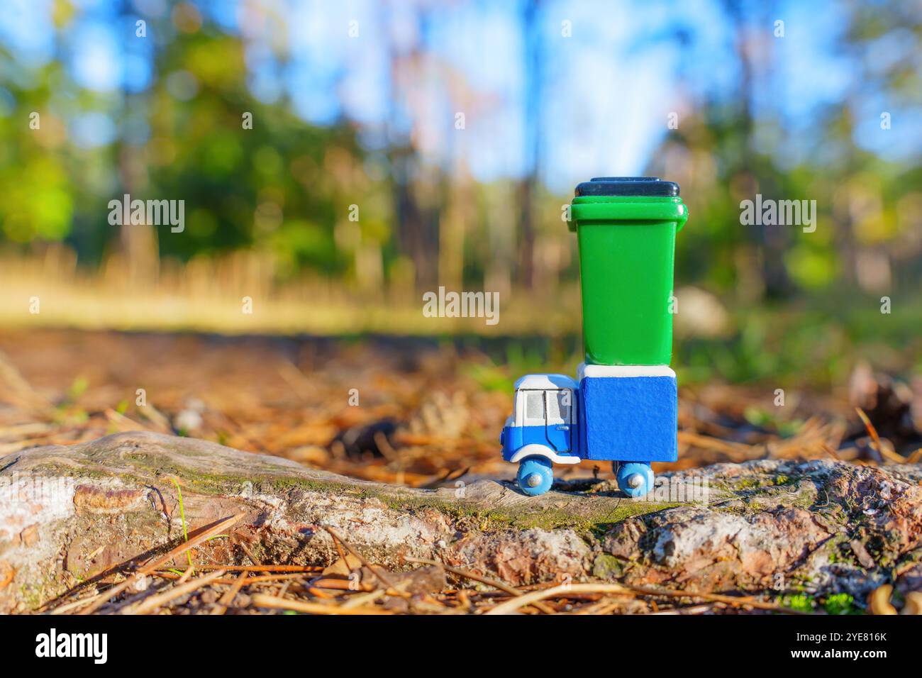 Toy truck carrying green garbage bin in a natural forest setting. Waste ...
