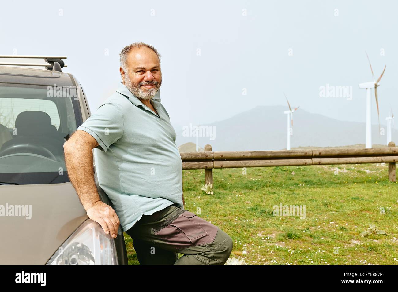 Man near the car looking on wind farm with mountain landscape view ...